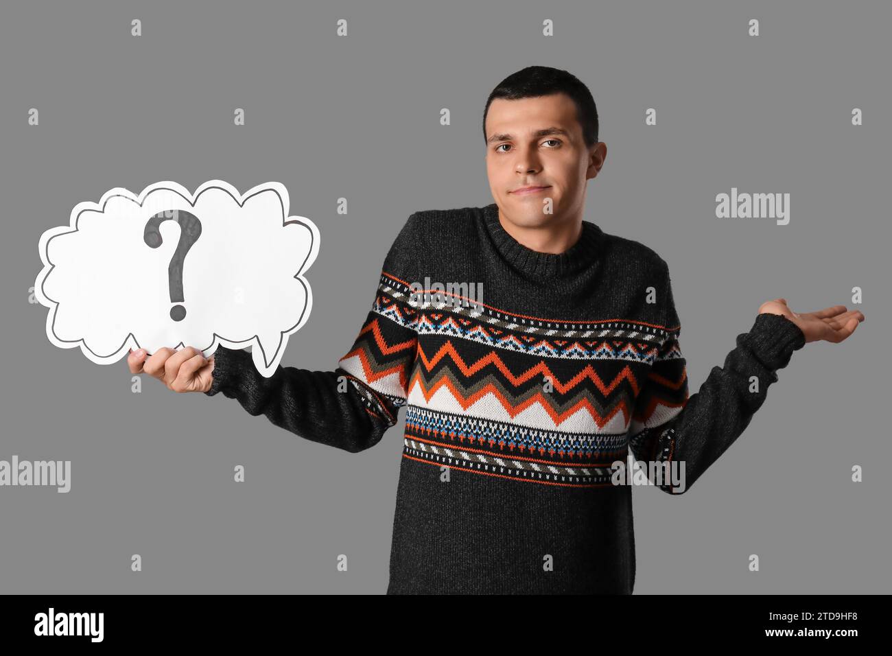 Wondering young man holding paper with question mark on grey background ...