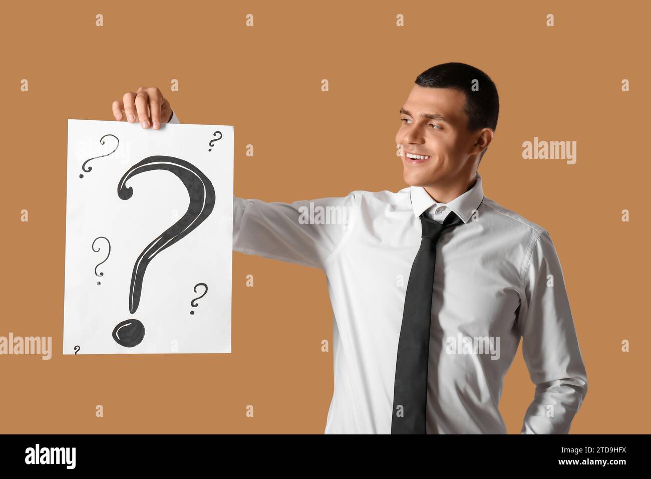 Young man holding paper with question marks on brown background Stock ...
