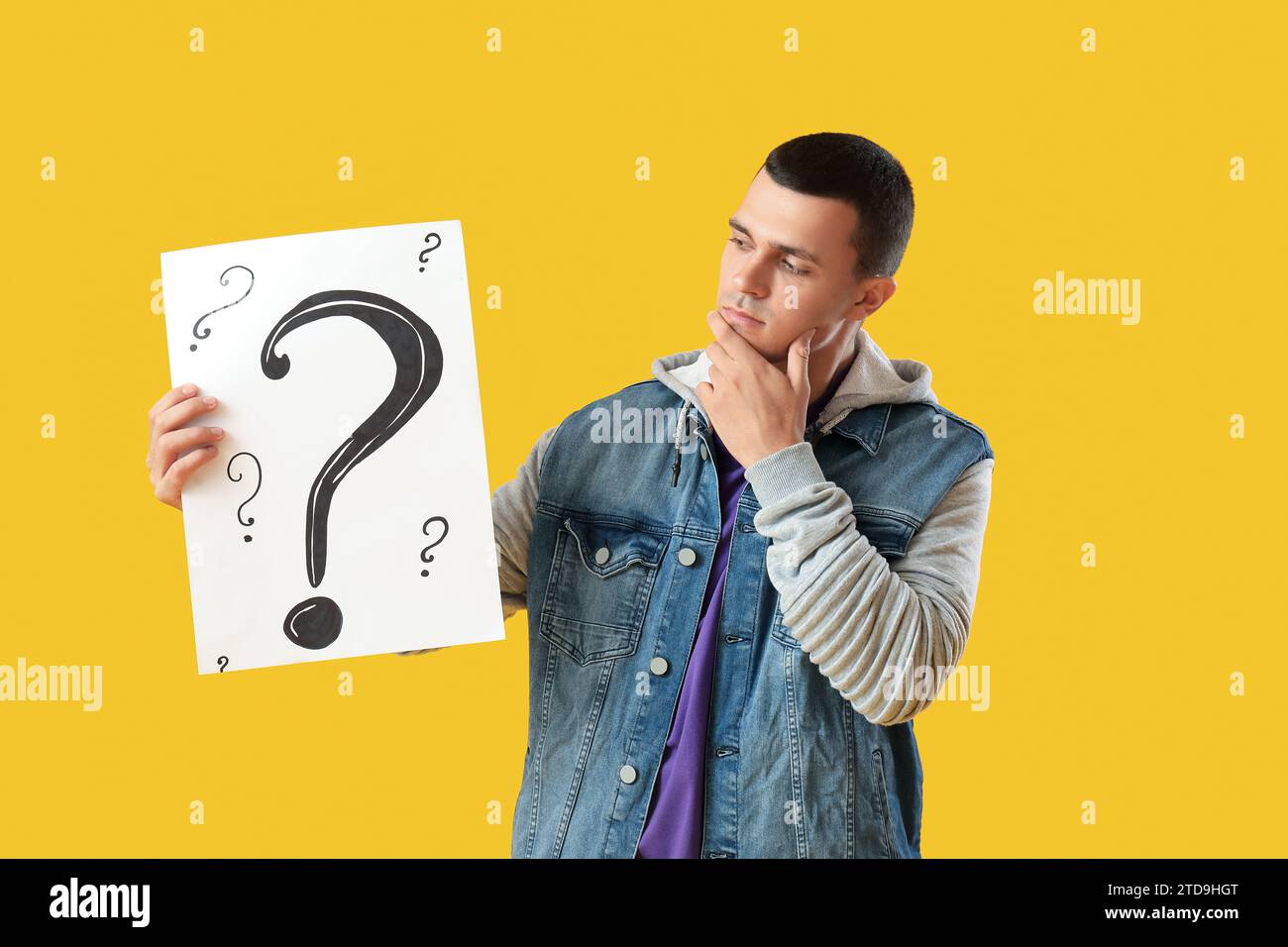 Wondering young man holding paper with question marks on yellow ...