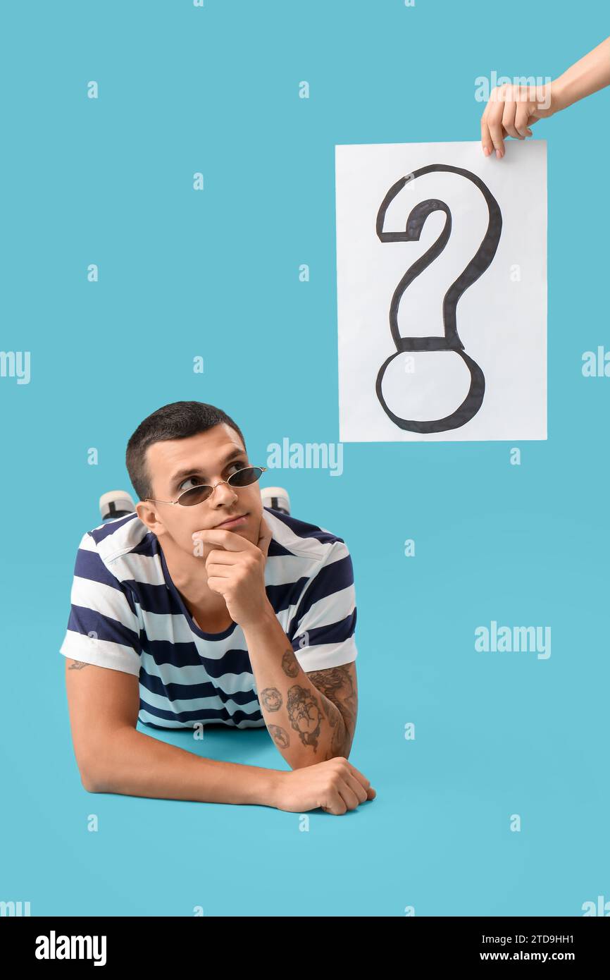 Young man and paper with question mark on blue background Stock Photo ...