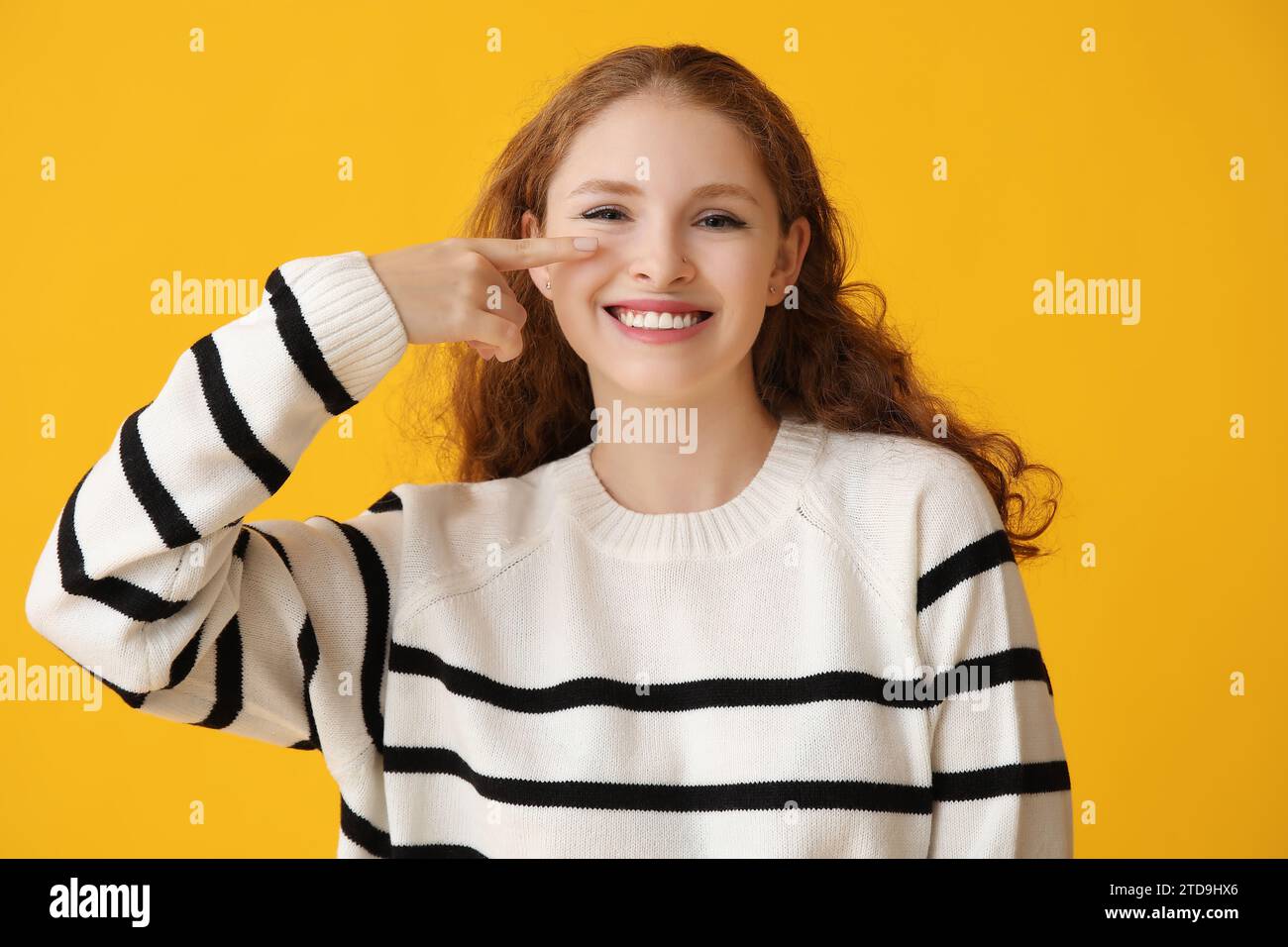 Portrait of pretty young girl pointing at her nose on yellow background ...