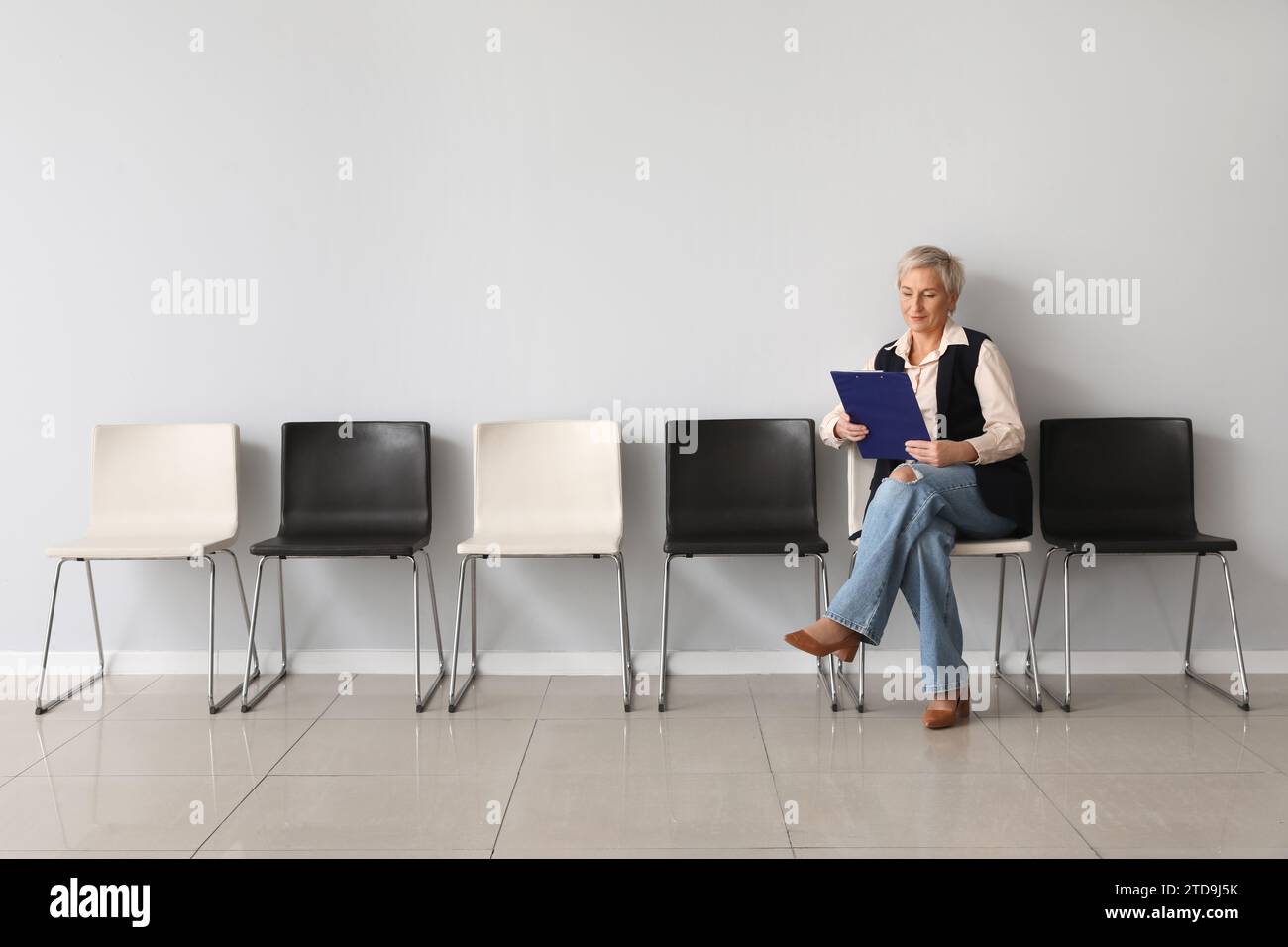 Mature female applicant with clipboard waiting for job interview near ...