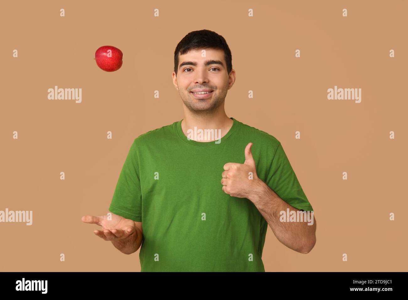 Young man with apple rich in vitamin A showing thumb-up on beige ...