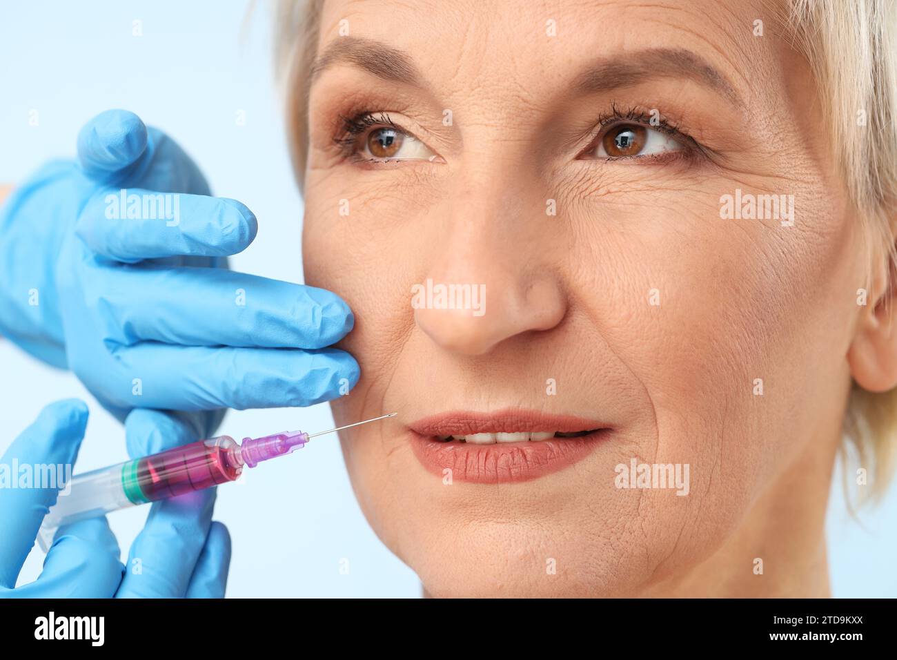Beautiful mature woman receiving lip injection on pink background ...