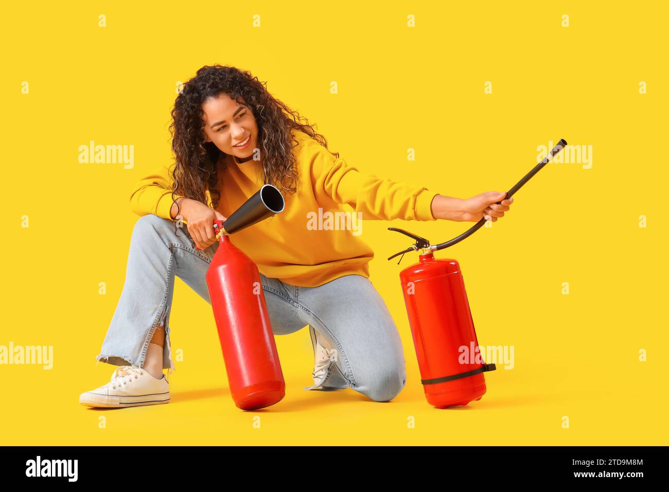 Young African-American woman with fire extinguishers on yellow ...