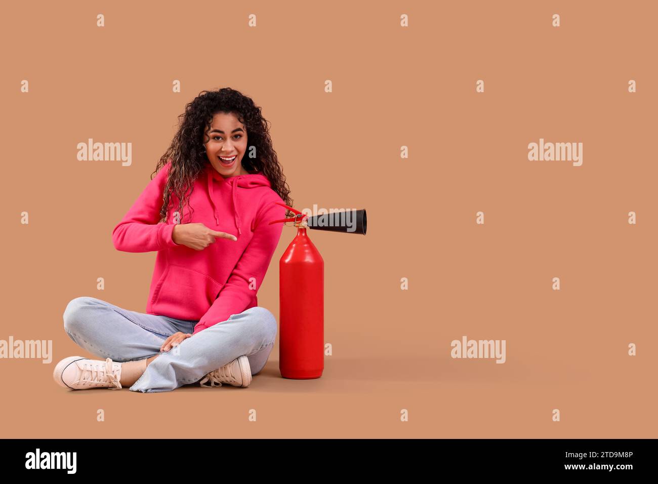 Young African-American woman pointing at fire extinguisher on brown ...