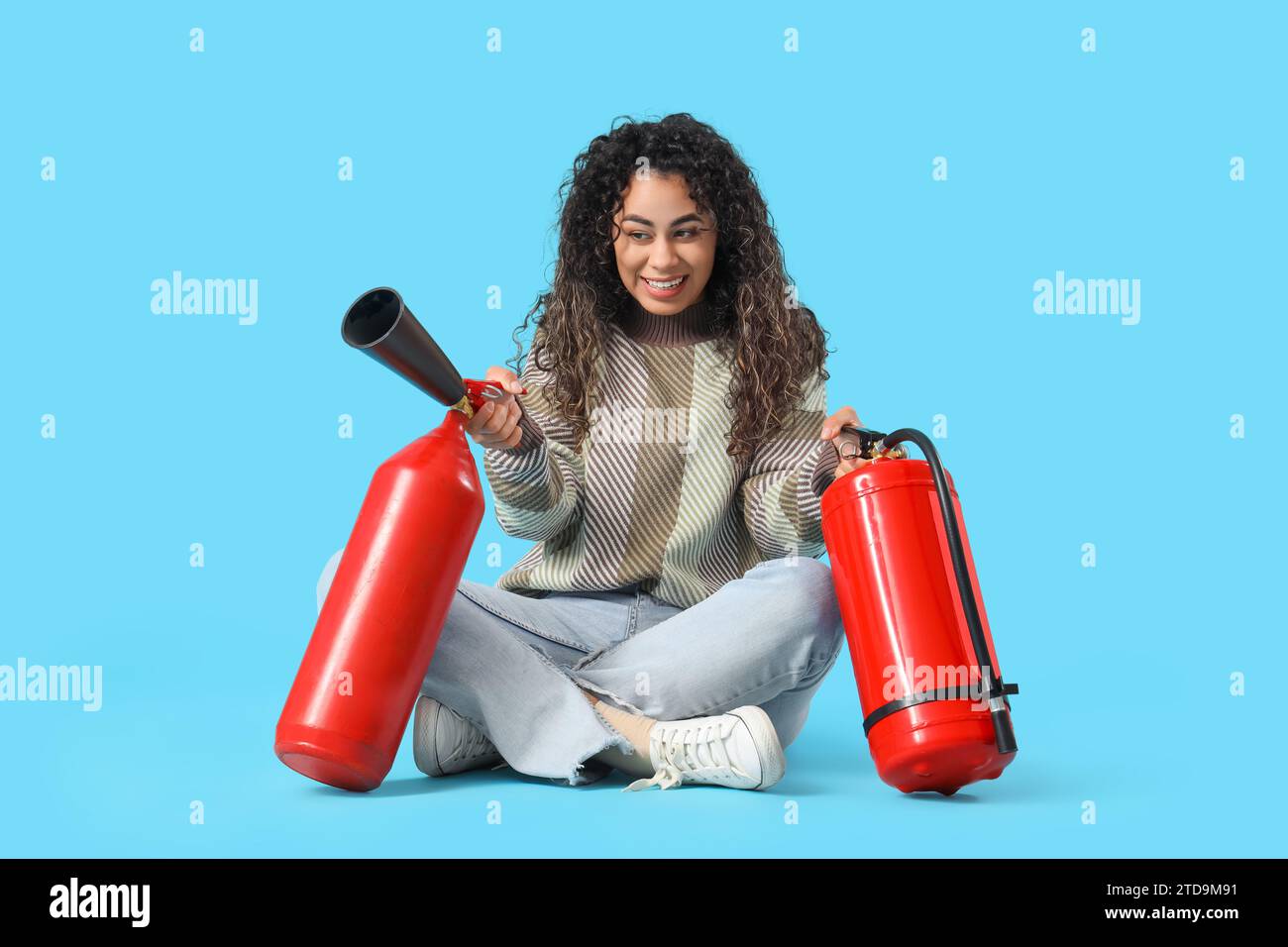 Young African-American woman with fire extinguishers sitting on blue ...