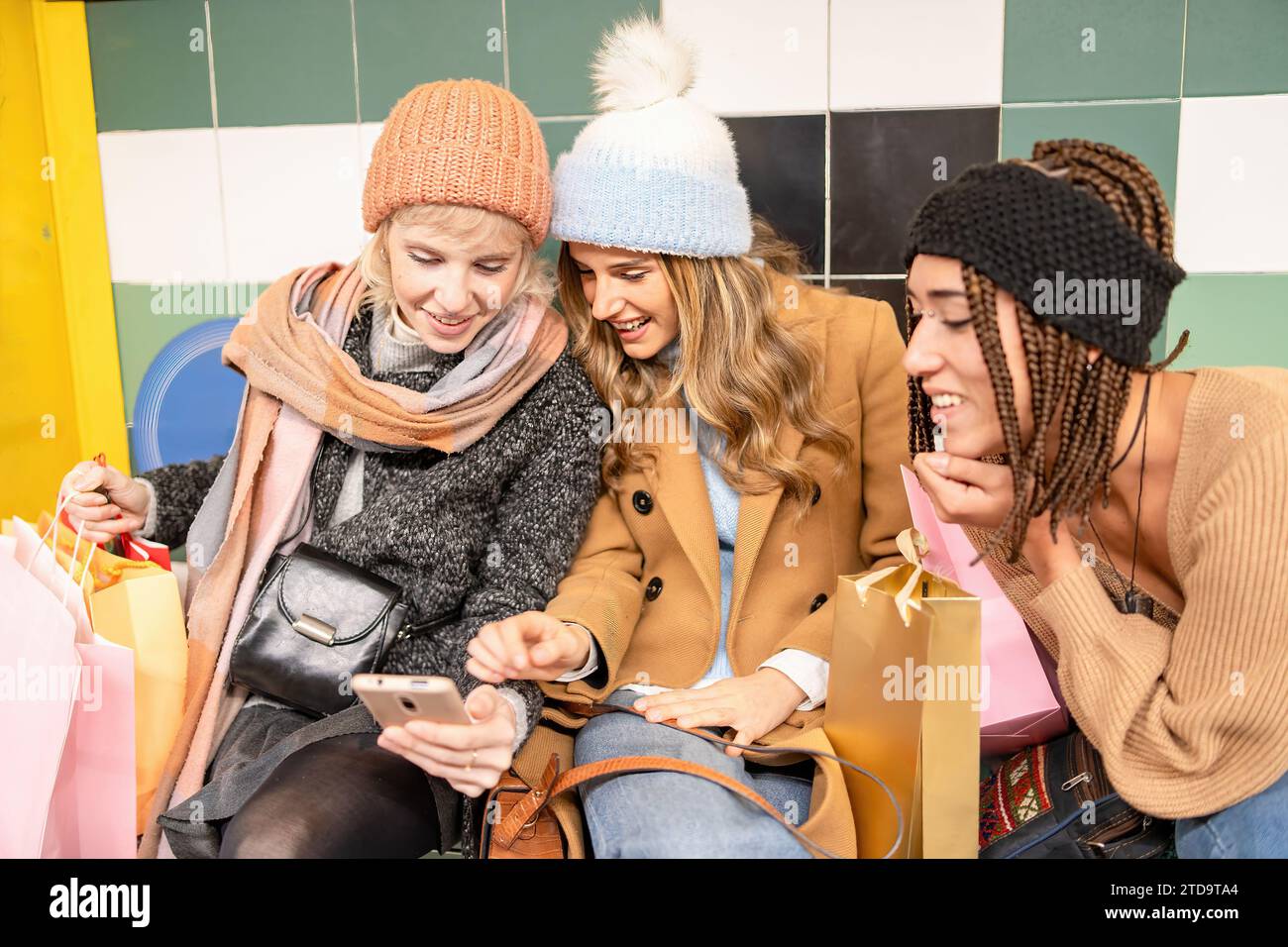 Three women laugh as they look at a smartphone together, enjoying a ...