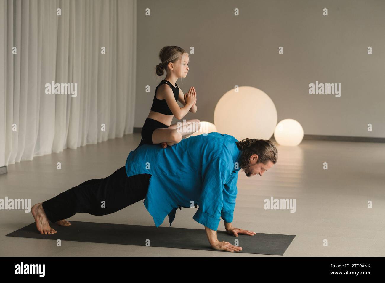 a child in the lotus position sits on the back of a yoga coach during ...
