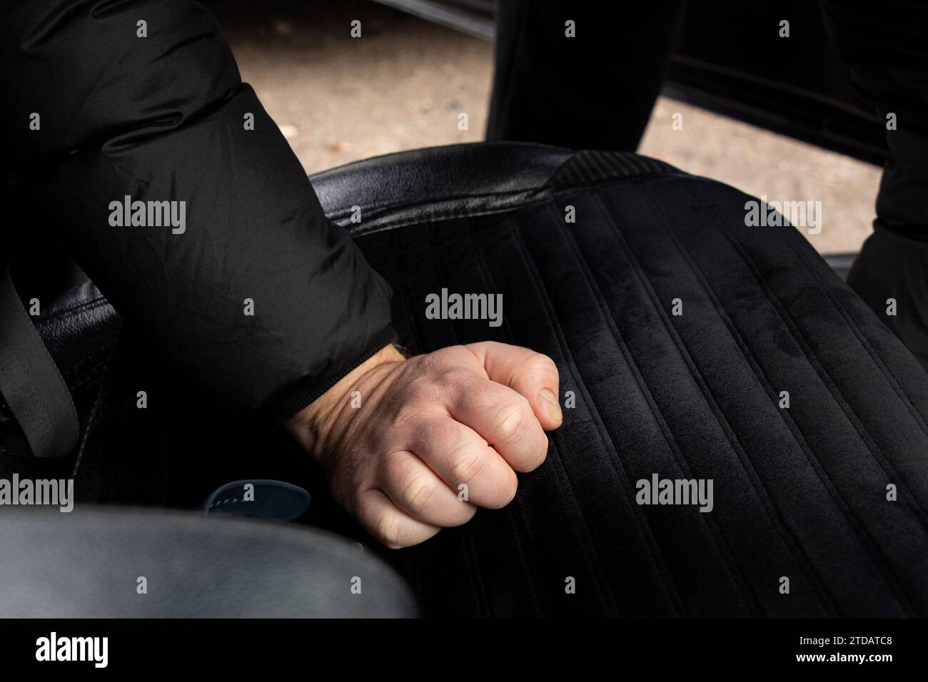 A man put his hand on the black driver's seat inside a car close-up ...