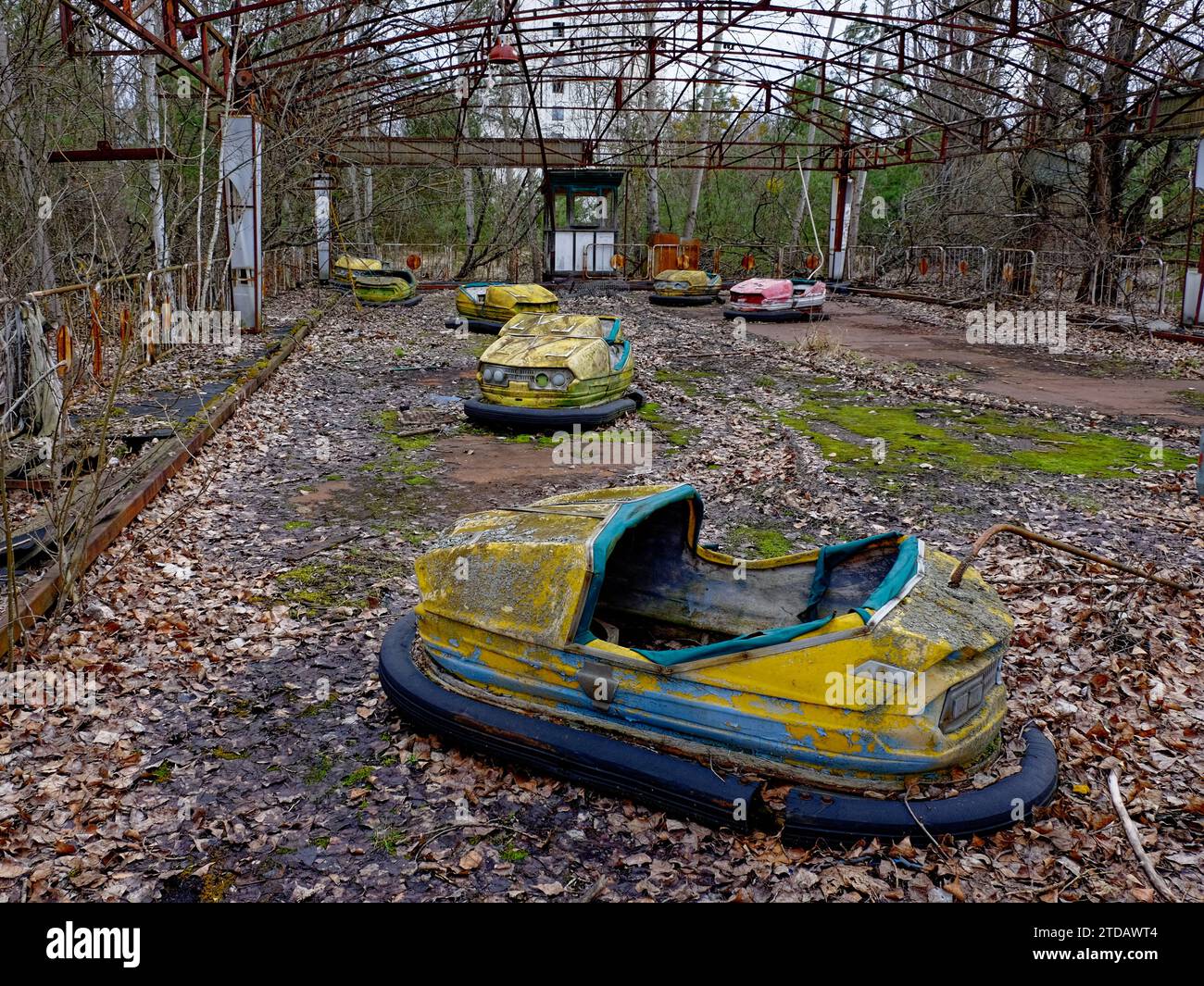 A rusted, abandoned yellow bumper car with empty seats surrounded by ...
