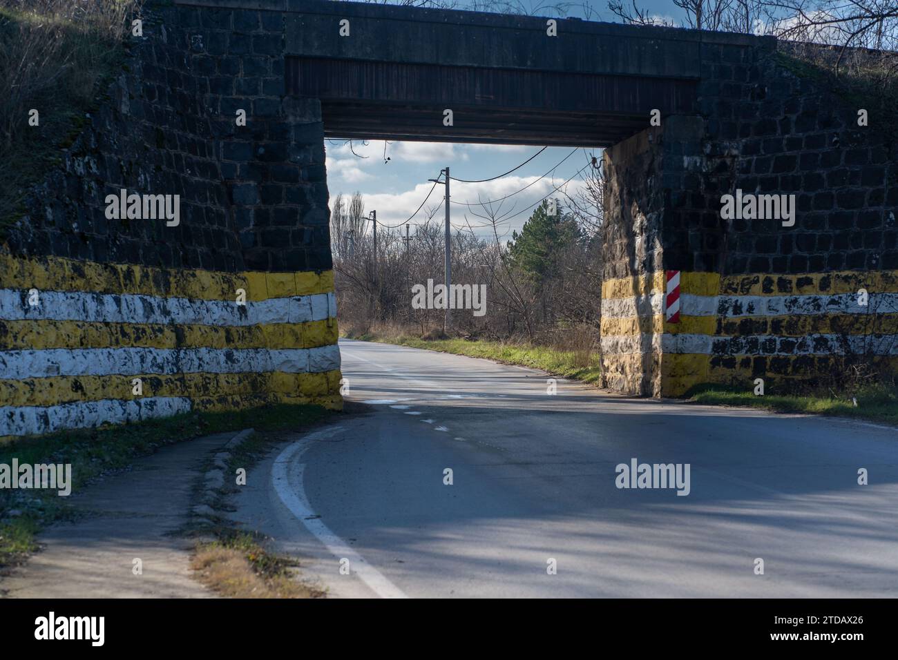 Asphalt road. Street narrow passage under stone bridge. Sunny day. Blue ...