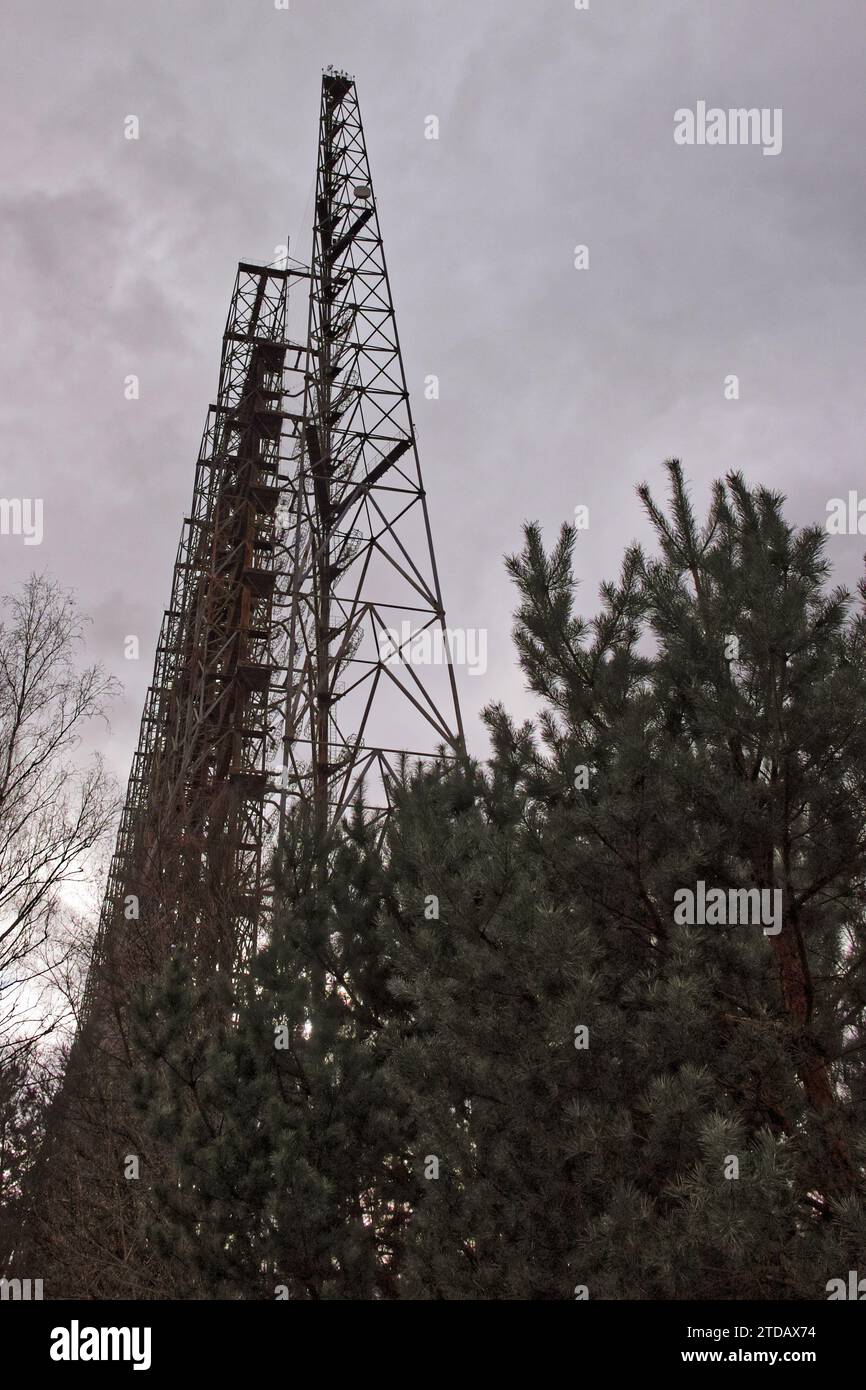 The image shows a tall, rusted metal tower standing amidst green trees ...