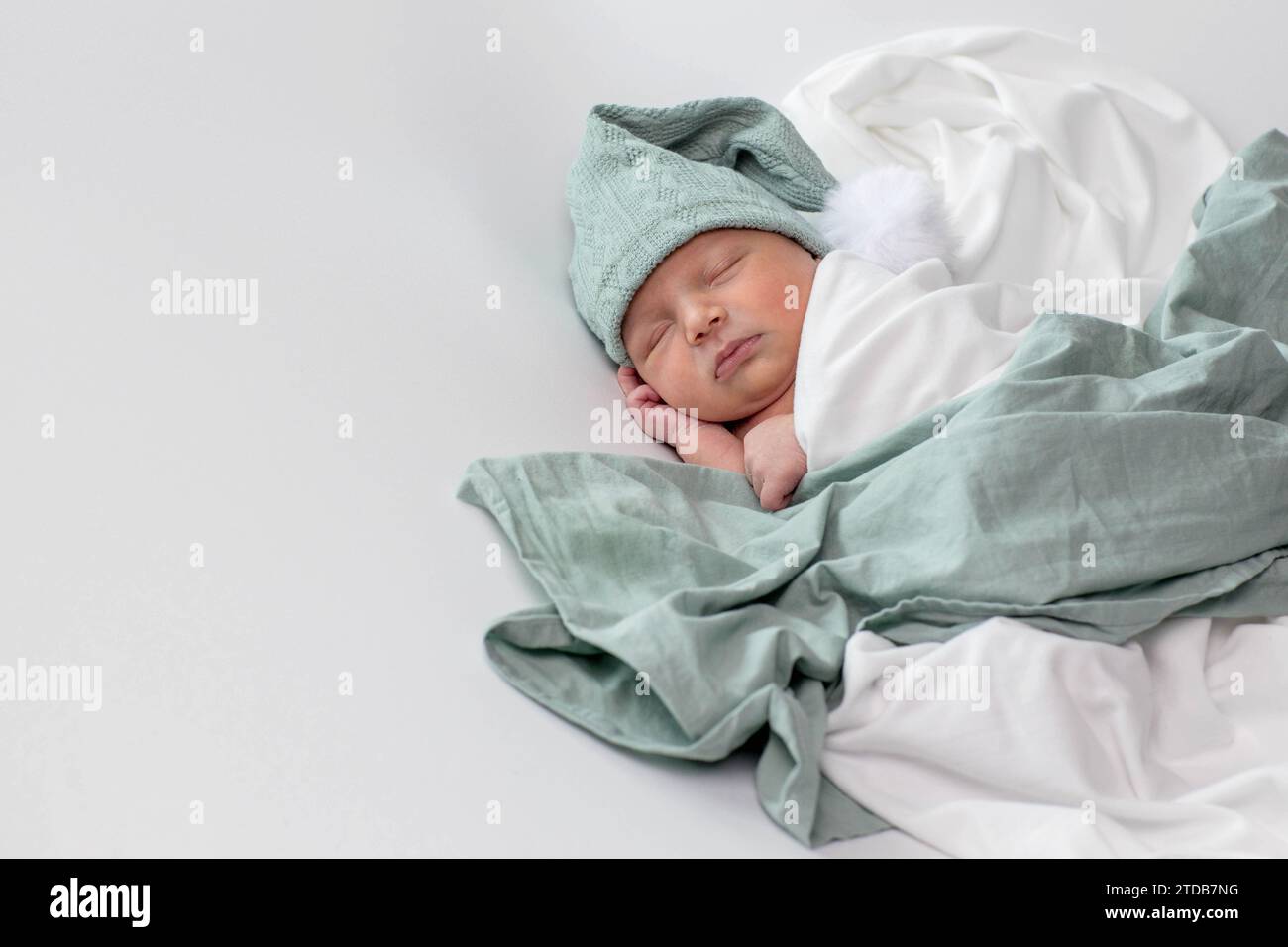 A 3-day-old baby wrapped in white cloth sleeping on a white background ...