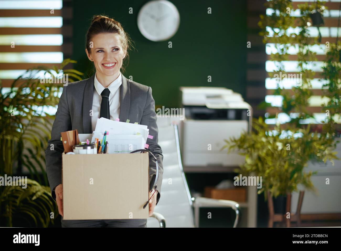New job. smiling modern female employee in modern green office in grey ...