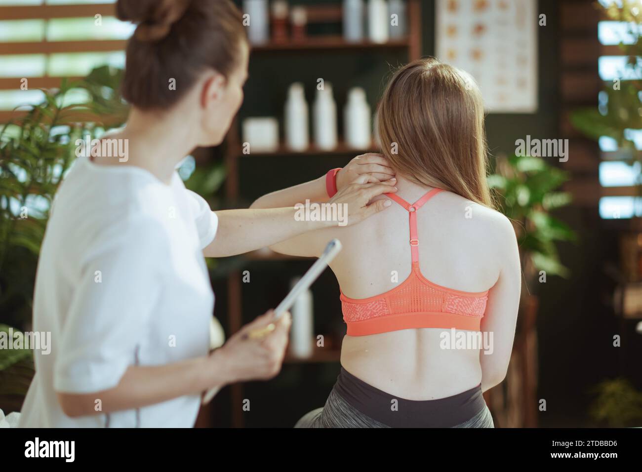 Healthcare time. Seen from behind female medical massage therapist in massage cabinet with ...