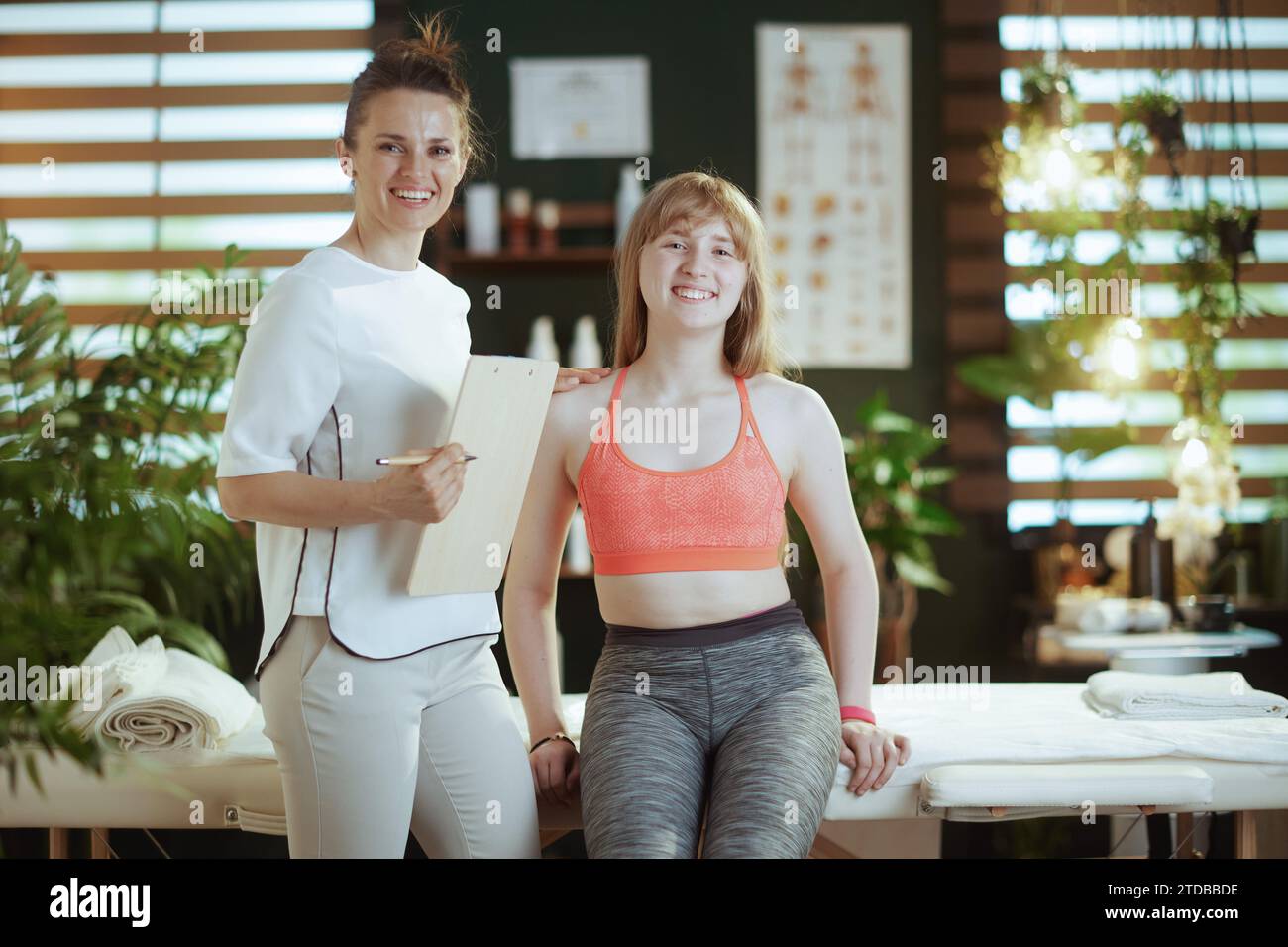 Healthcare time. smiling female massage therapist in massage cabinet with clipboard and teenage ...