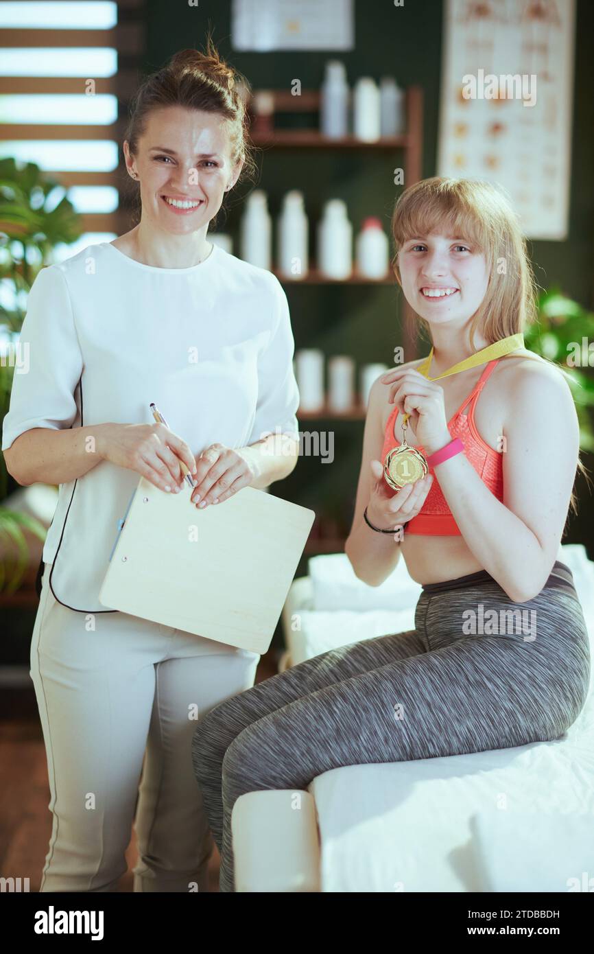 Healthcare time. happy massage therapist woman in massage cabinet with clipboard, teenage client ...