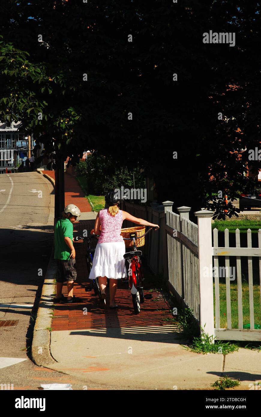 A mother and son walk their bikes on a narrow stretch of sidewalk in ...