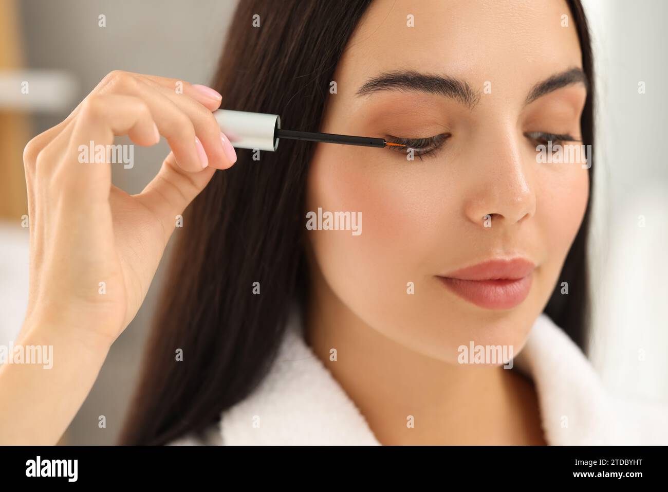 Beautiful woman applying serum onto her eyelashes indoors, closeup ...