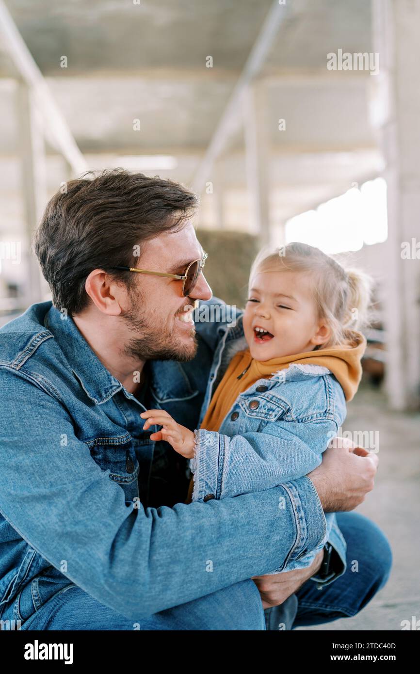 Smiling dad hugging a little girl laughing loudly while squatting near ...