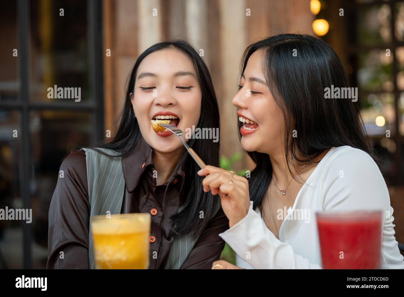 A lovely and cheerful Asian girl is feeding food to her female friend ...