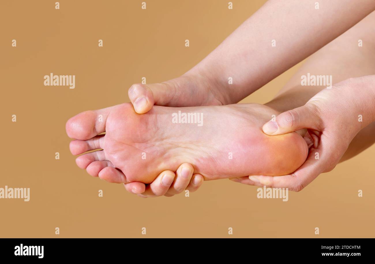 Woman with severe plantar pain is massaging her foot, isolated on beige ...