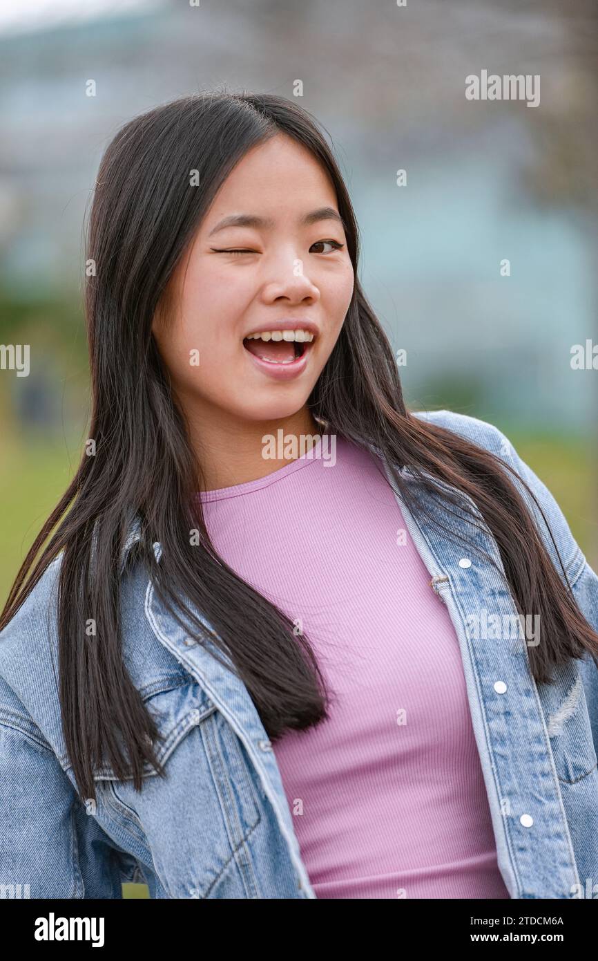 Portrait of young Asian woman winking an eye and smiling while posing ...
