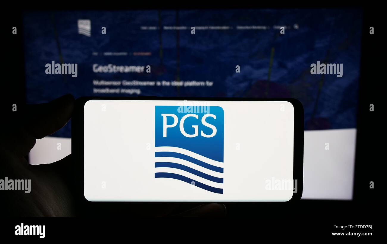 Person holding mobile phone with logo of Norwegian oilfield service company PGS ASA in front of ...