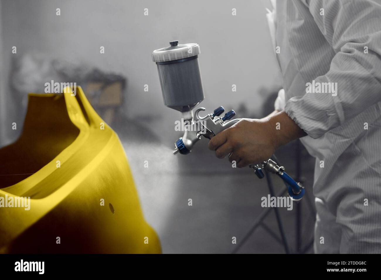 Professional male car painter sprays paints car part to gold color in ...