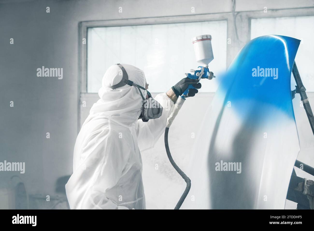 Professional spray painter in protective mask and clothes spraying car ...