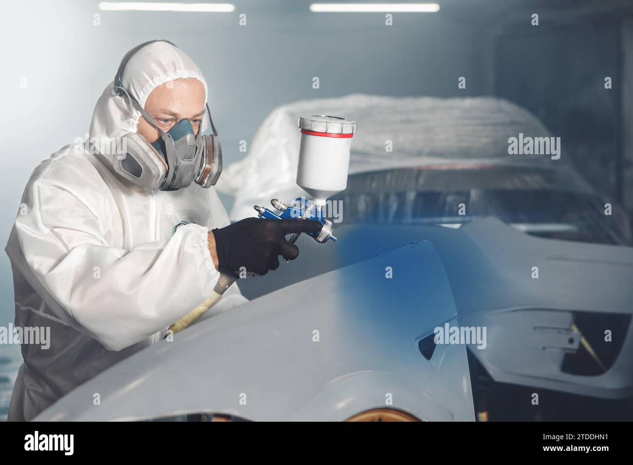 Car paint worker spraying blue paint to car body element using spray ...