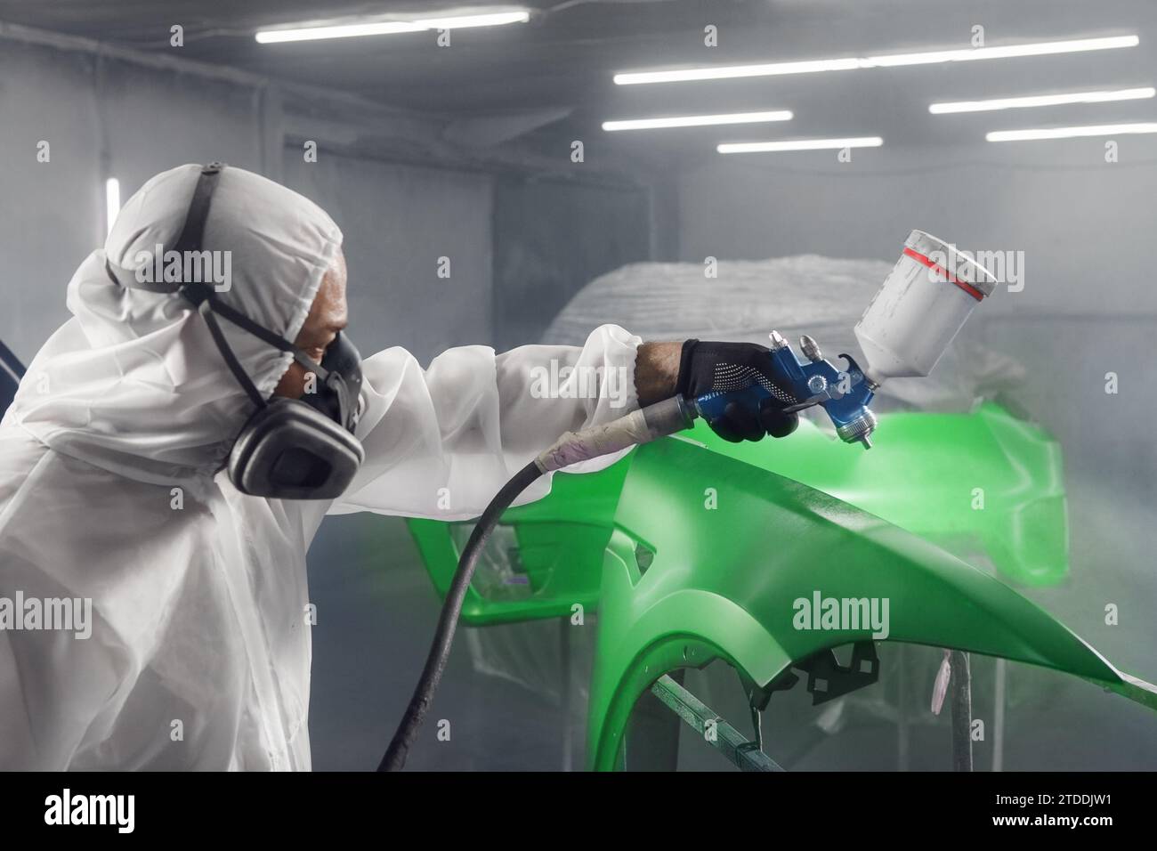Car paint worker spraying green paint to car body element using spray ...