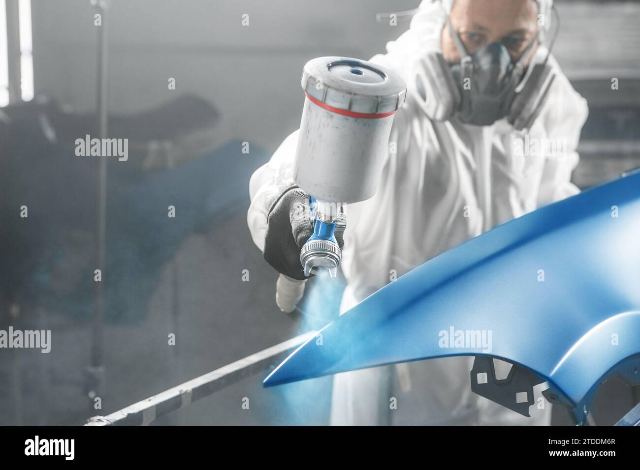 Car paint worker spraying blue paint to car body element using spray ...