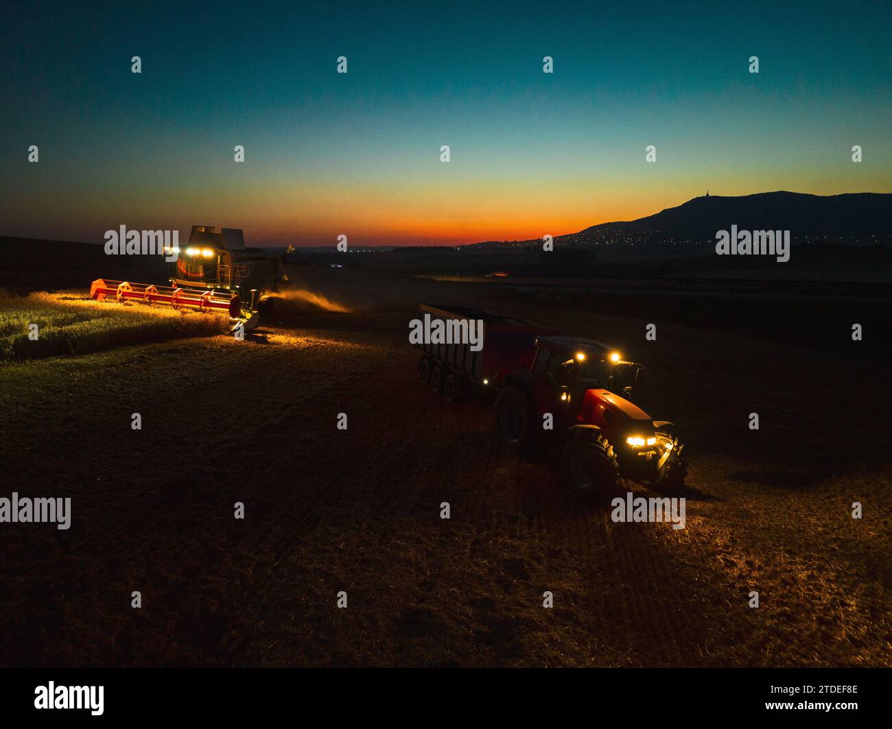 Aerial view of a tractor and harvester working in a field during night ...