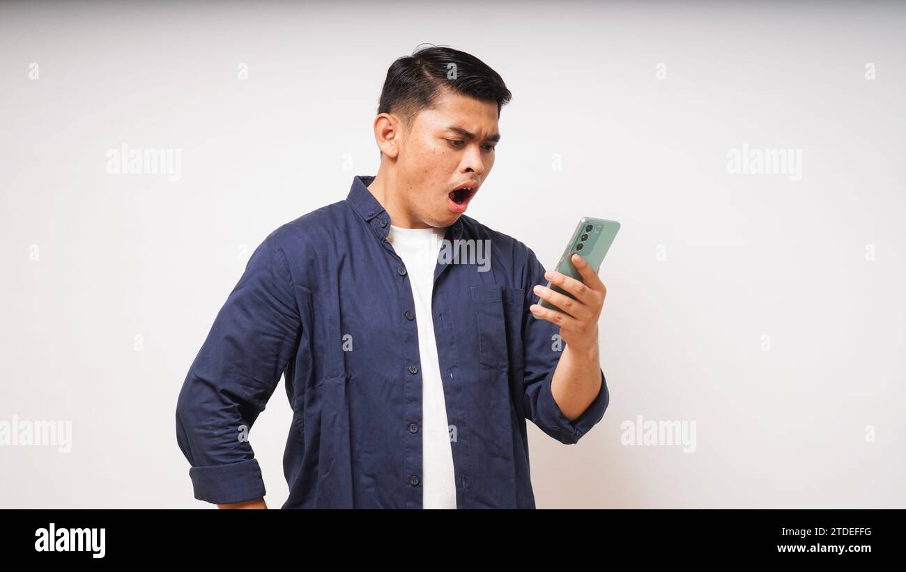 Young Asian man showing shocked face expression while using mobile ...