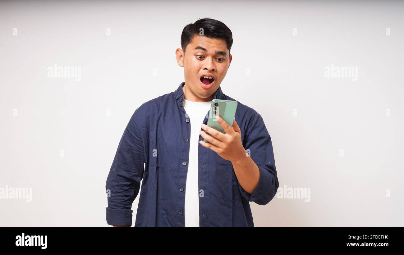 Young Asian man showing shocked face expression while using mobile ...