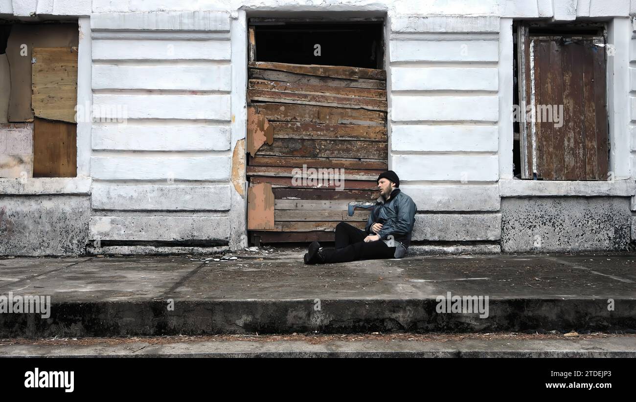 Illegal caucasian immigrant sits on ground. Below poverty line ...