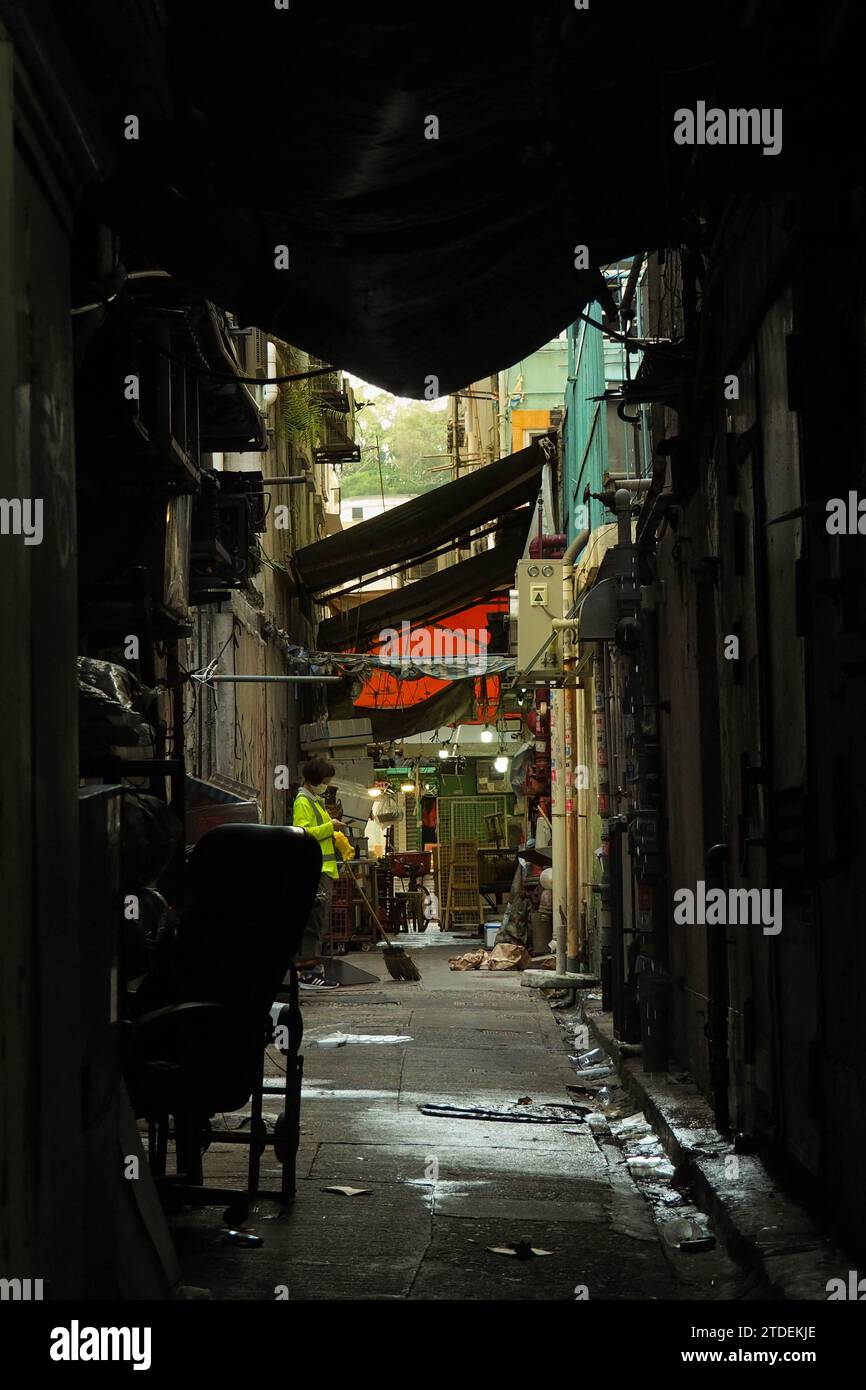 A dark alleyway hidden behind the streets of Hong Kong, with a woman in ...