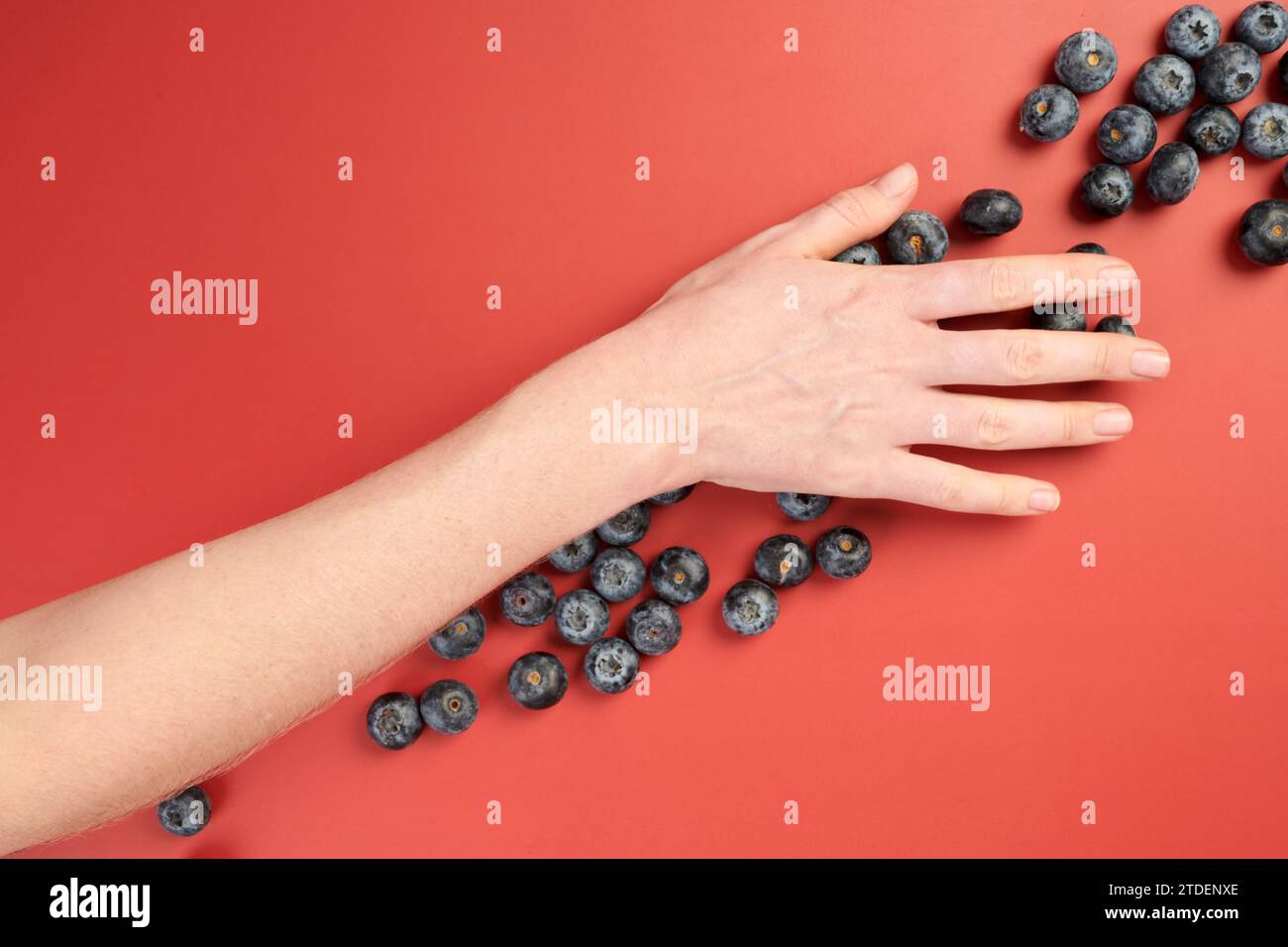 Hand grabbing blueberries from red table, top view Stock Photo - Alamy