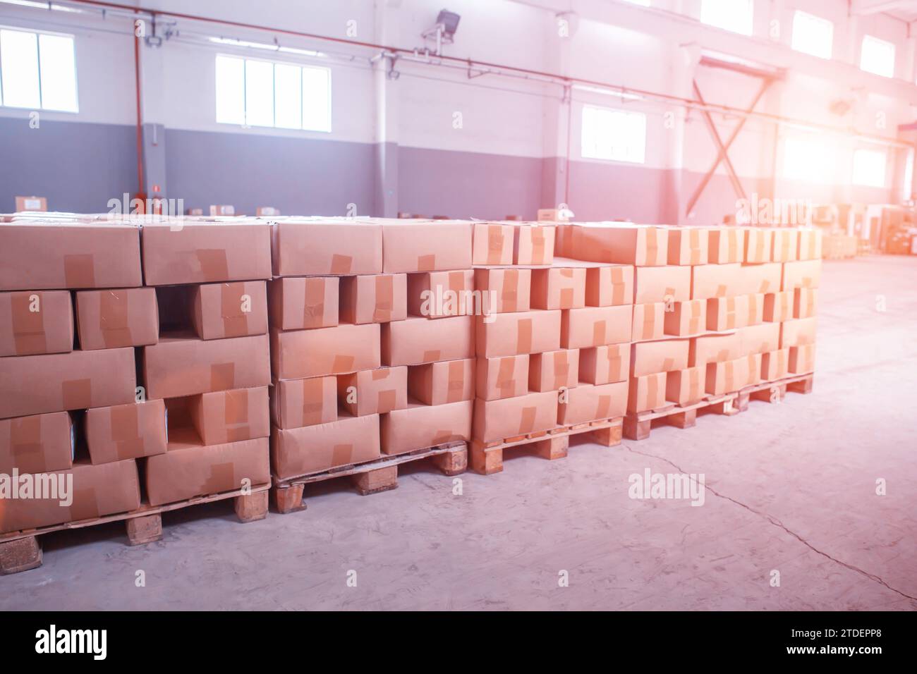 Many cardboard boxes on pallets in a warehouse against a sunset ...