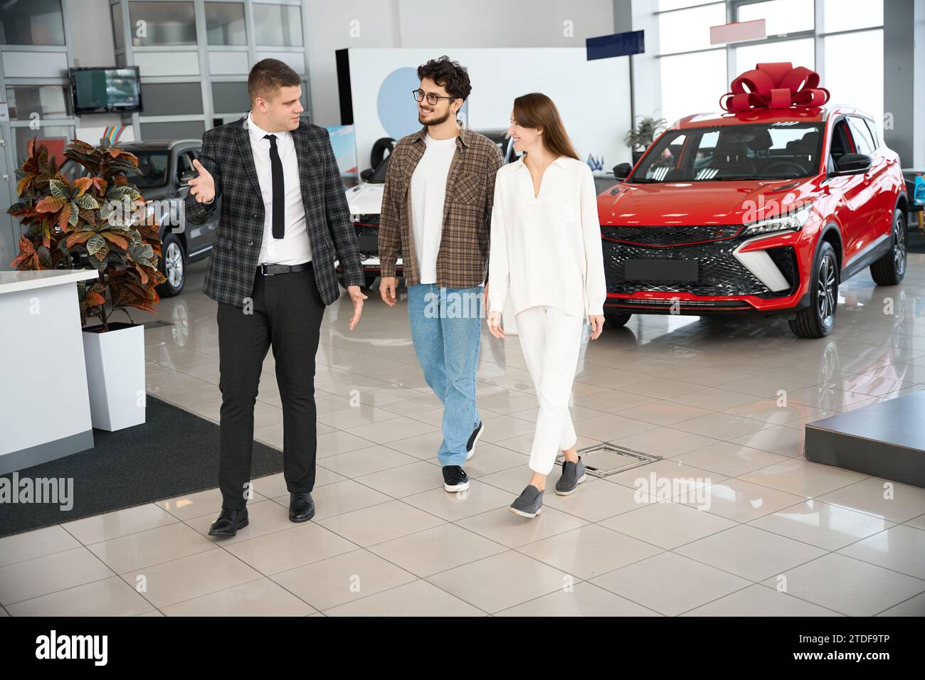 Couple and dealer walking around showroom choosing car for woman as ...
