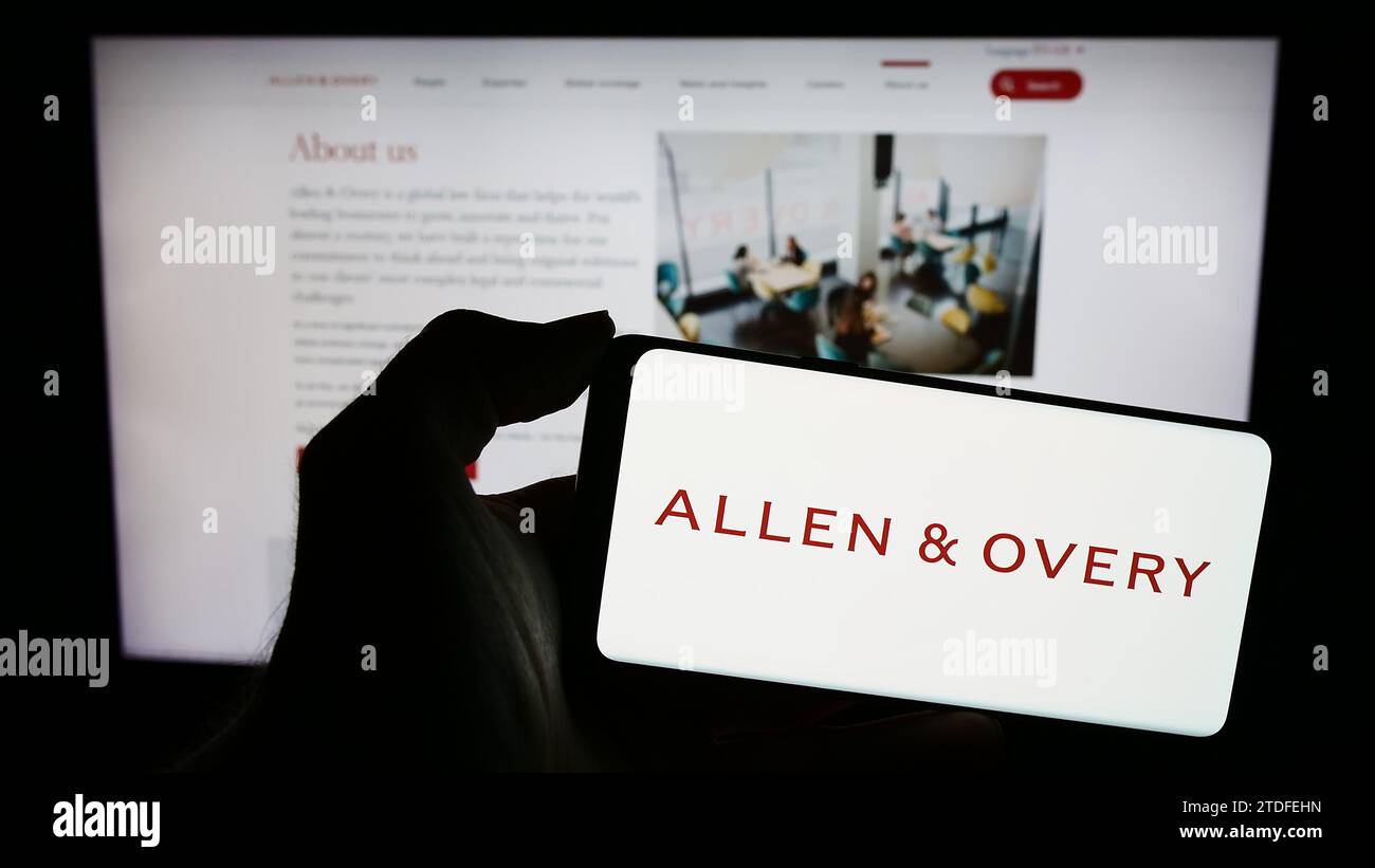 Person holding smartphone with logo of British law firm Allen and Overy LLP in front of website ...