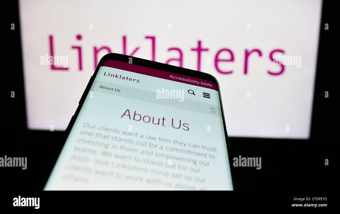 Mobile phone with website of British law firm Linklaters LLP in front of business logo. Focus on ...