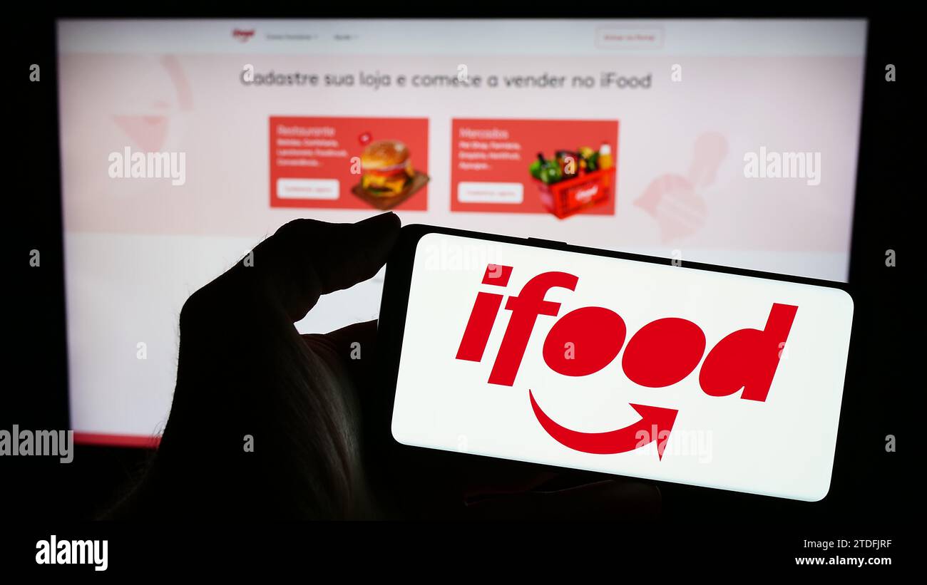 Person holding mobile phone with logo of Brazilian food ordering and ...