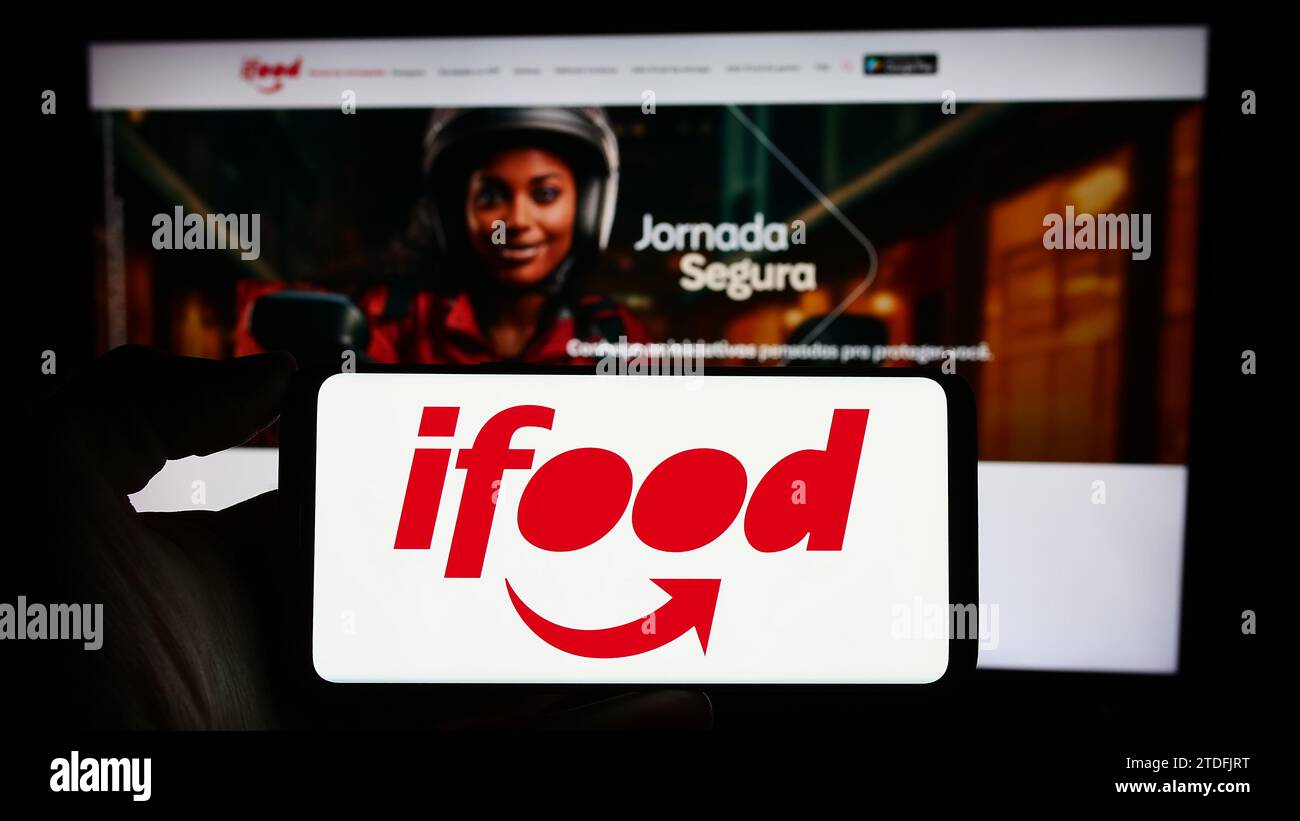 Person holding cellphone with logo of Brazilian food ordering and ...