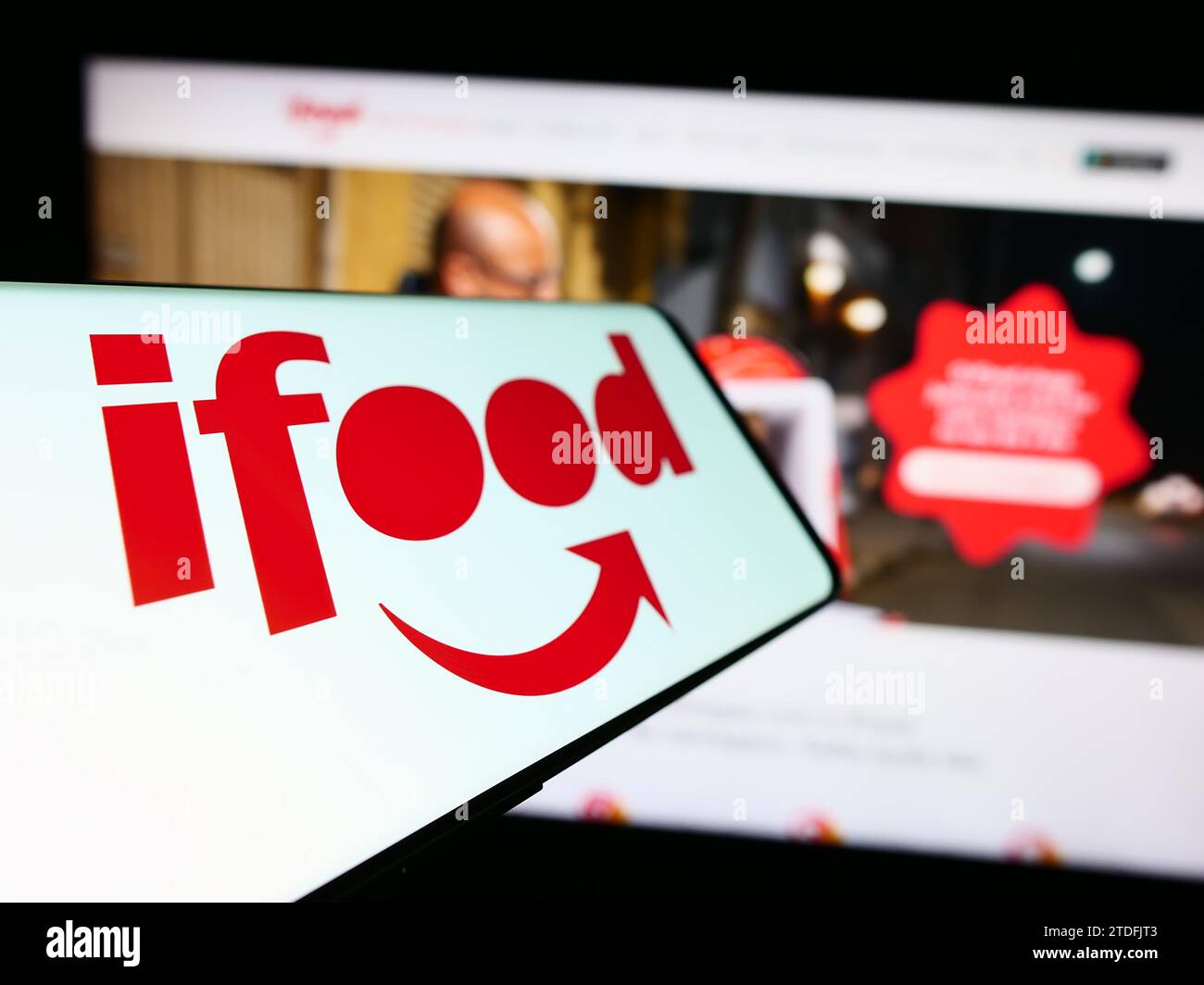 Cellphone with logo of Brazilian food ordering and delivery company iFood in front of business ...