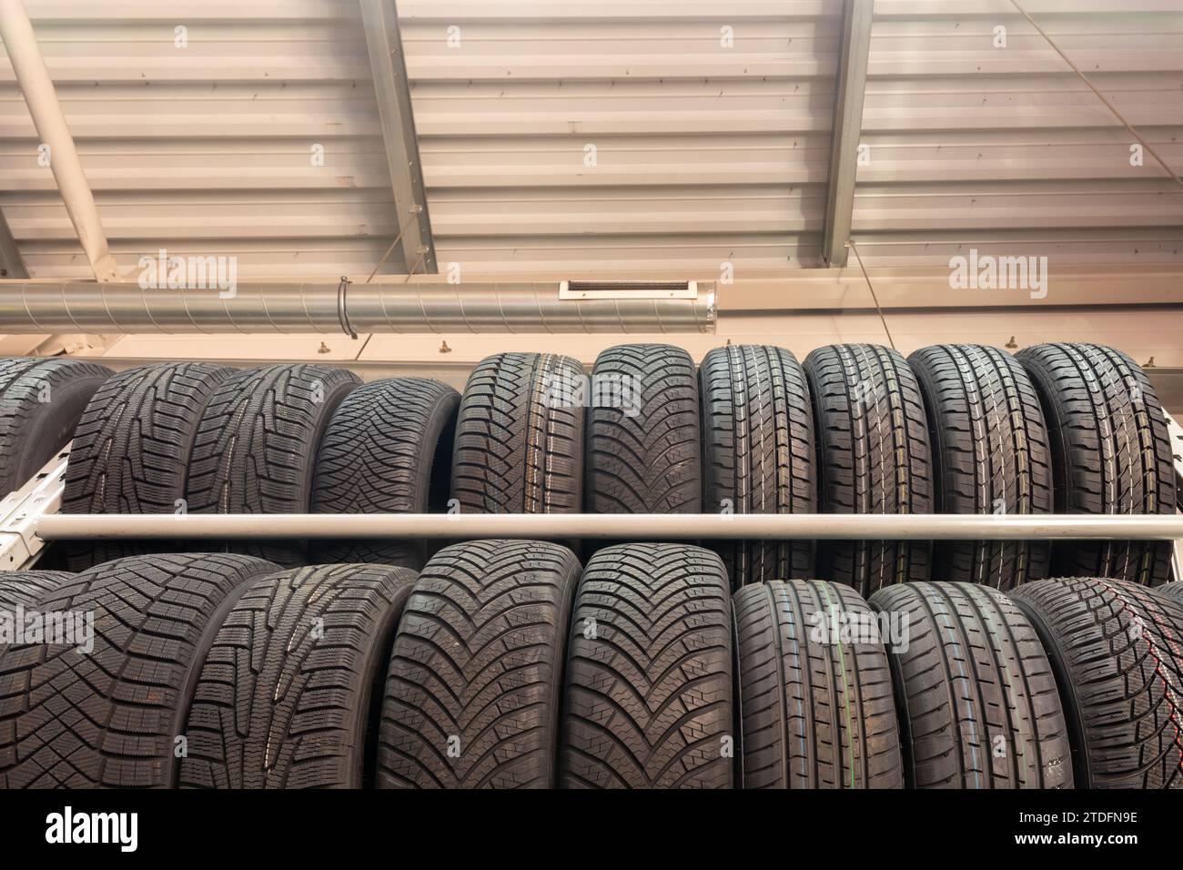 Car tires on rack in auto store. Two rows of tires on the shelves in the store against the ...