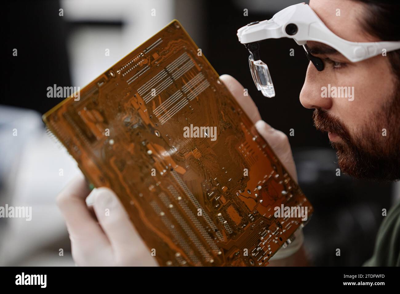 Side view closeup of repairman inspecting circuit board with magnifying ...