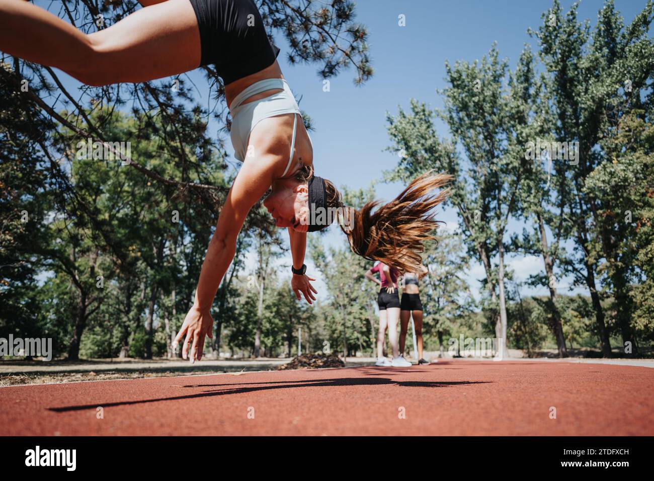 Active girls doing cartwheels in a sunny park, showcasing their fit bodies and enjoying a fun ...